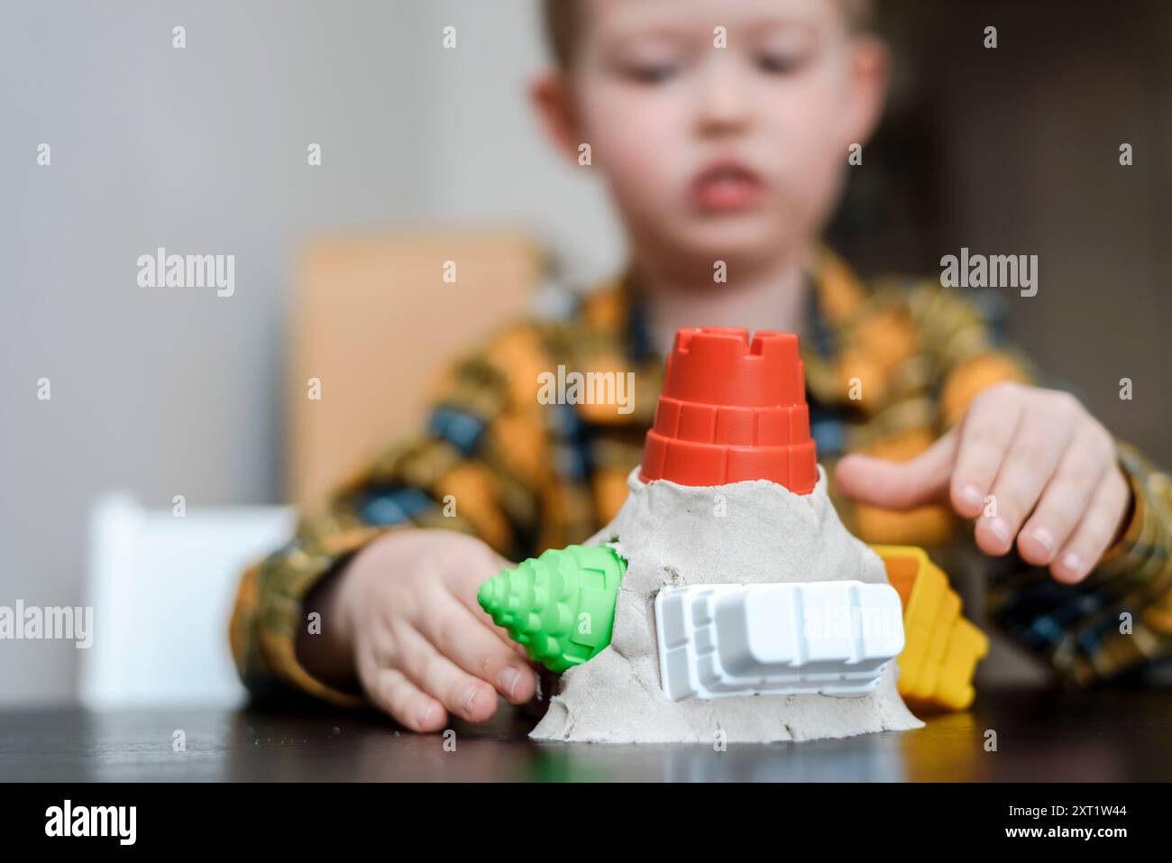 A good boy makes a tower of kinetic sand at home. The child plays in ...
