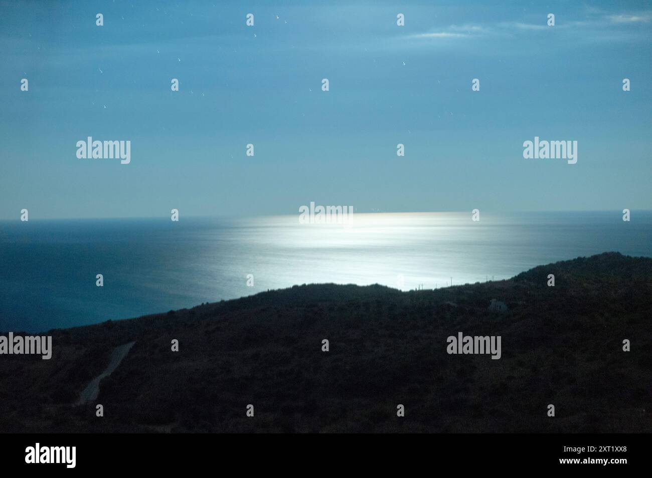 Moonlight reflects over a calm sea beyond a silhouetted coastline under ...