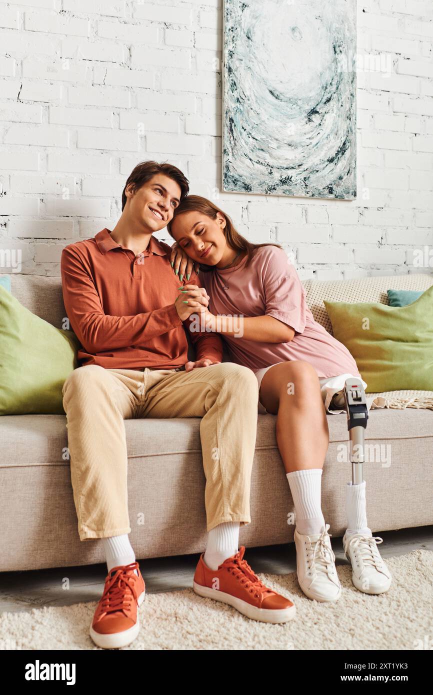 A young couple sits on a couch, the woman resting her head on her ...
