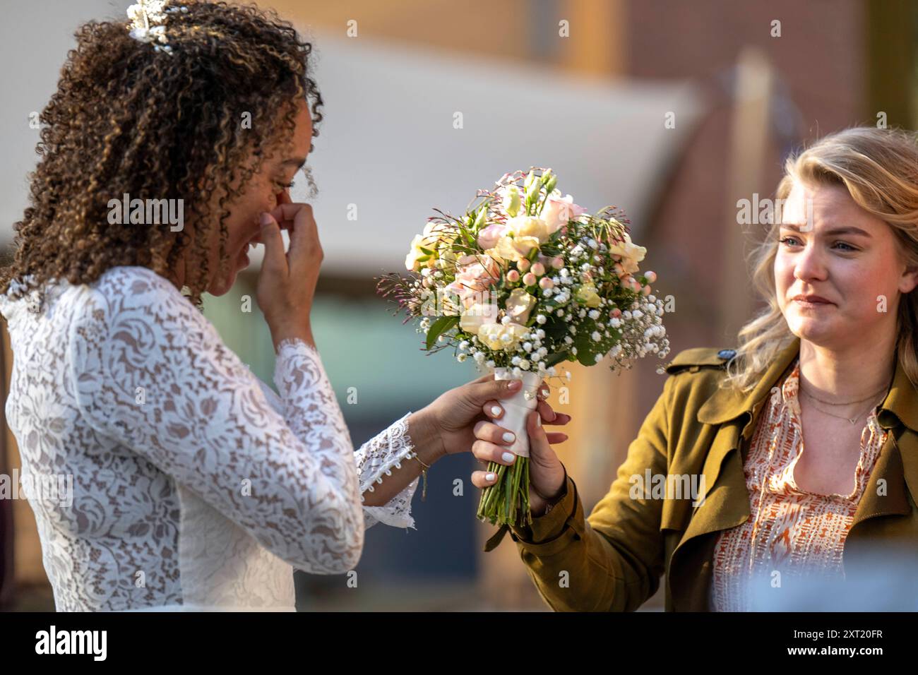 Emotional bride in lace dress wiping away tears while holding a bouquet ...