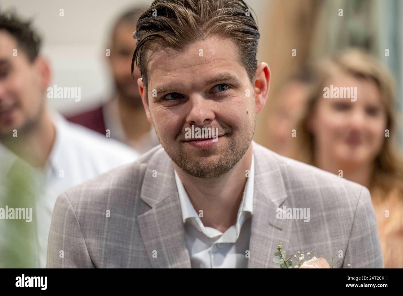 A groom in a gray checkered suit with a boutonniere smiles at a wedding ...