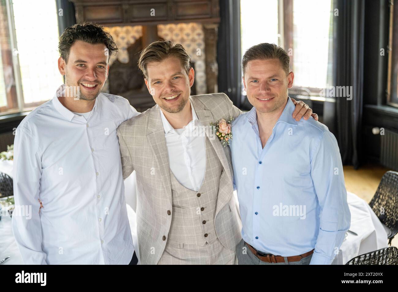 Three smiling men dressed in formal attire posing together indoors ...