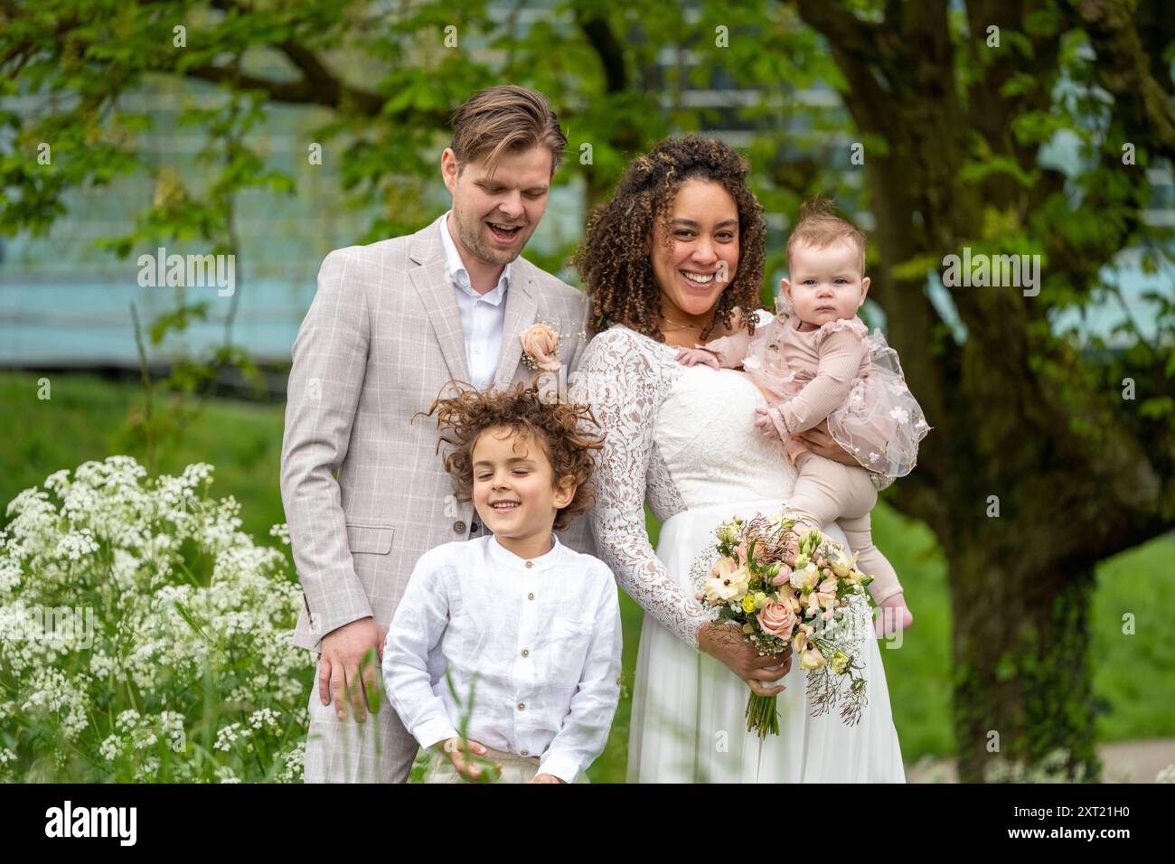 A well-dressed family posing for a photo outdoors with blooming flowers ...