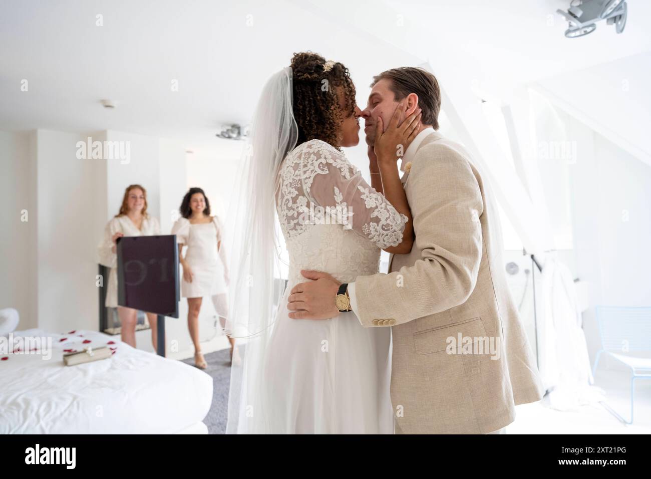Bride in a lace dress and groom in a beige suit share a kiss in a ...