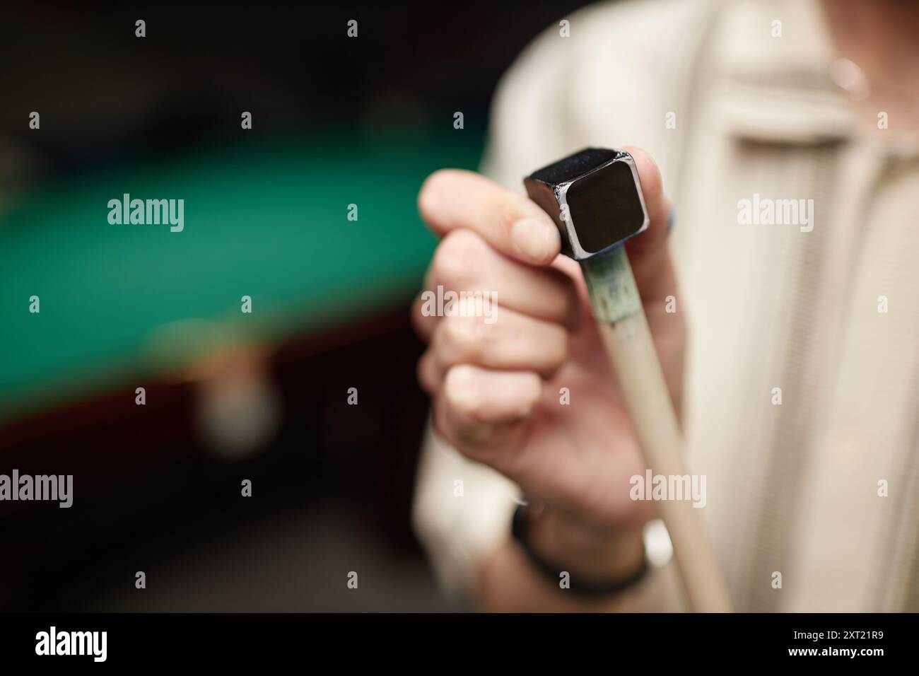 Hand holding a pool cue with a chalked tip in focus, blurred background ...
