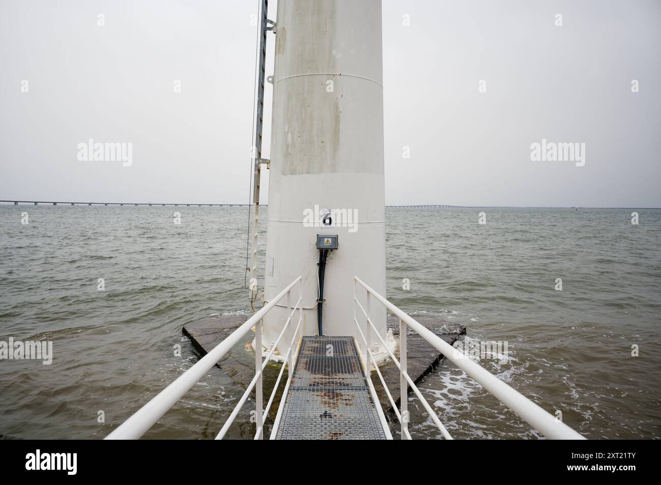 A lone pillar stands anchored in the Tagus River, with a distant bridge ...