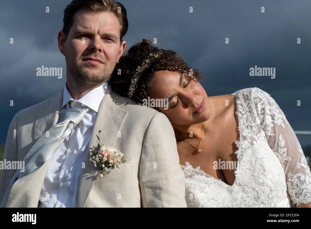 Bride leaning on groom s shoulder under a dramatic cloudy sky, both ...