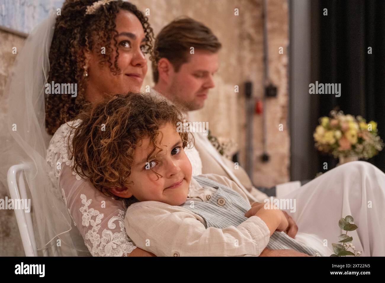 A bride in a lace wedding dress lovingly gazes aside while a young boy ...