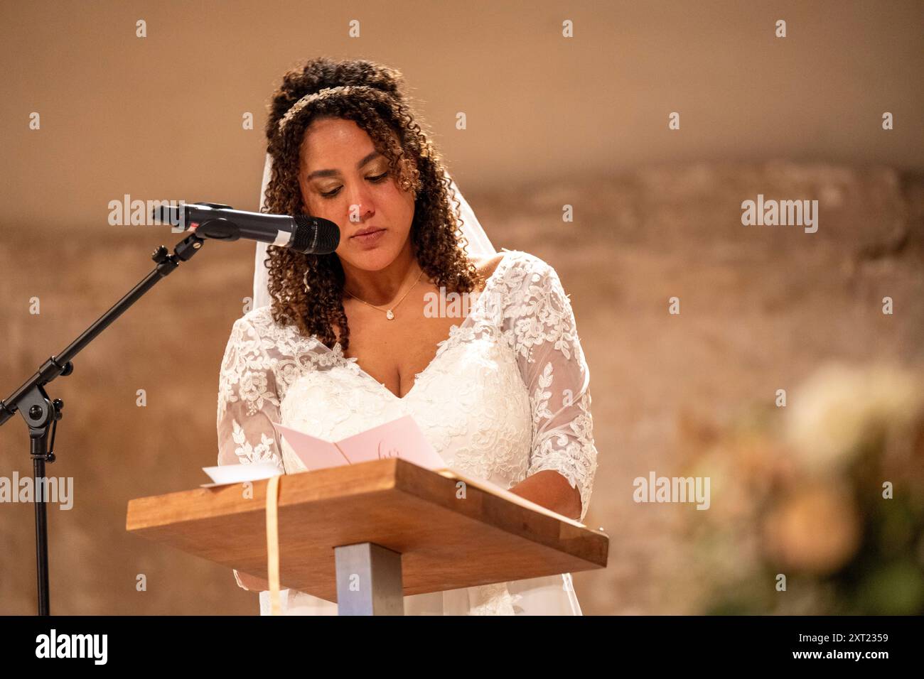 Bride in a lace wedding dress delivering a heartfelt speech at a podium ...
