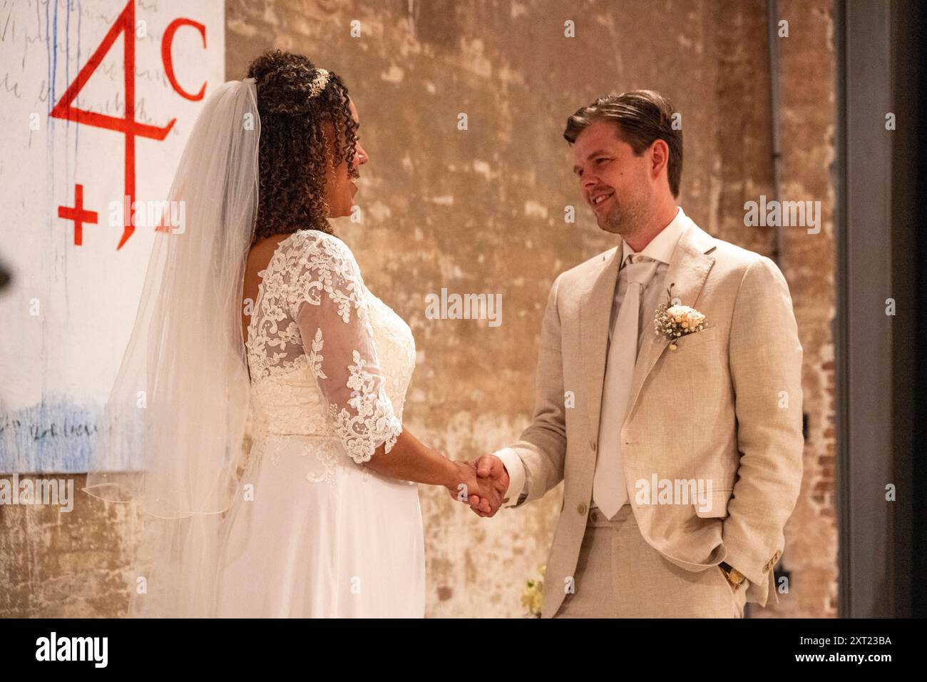 Bride and groom hold hands during wedding ceremony with a graffiti art ...