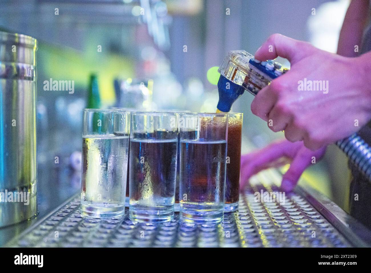 Bartender pouring a blue liquid into shot glasses on a bar counter with ...