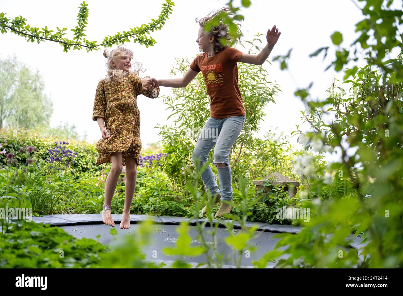 Two people jumping on a trampoline in a lush garden. panc06125 ...