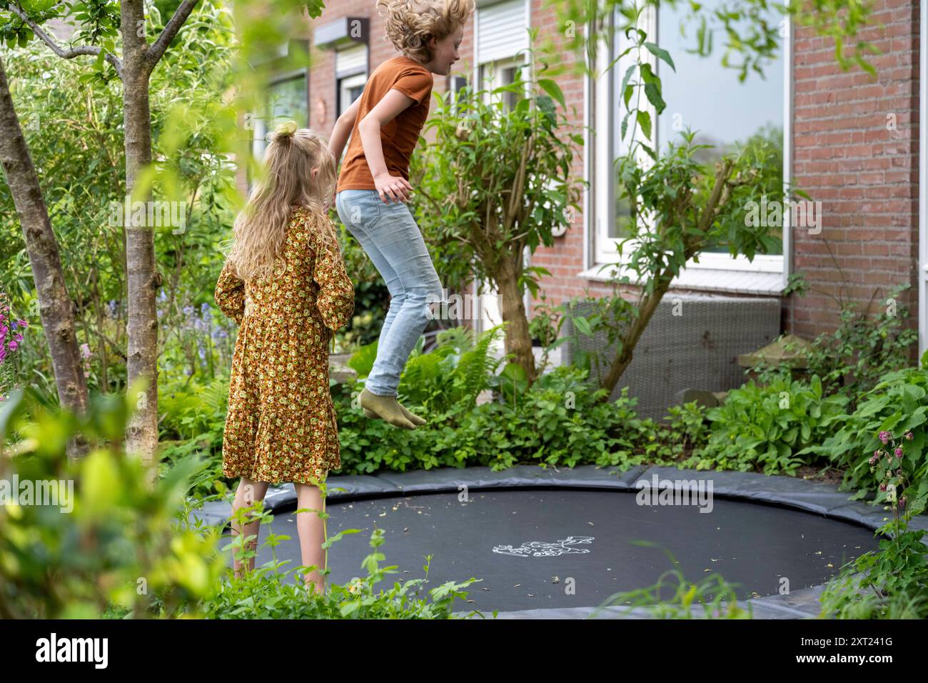 Children playing on a garden trampoline with a house and greenery in ...