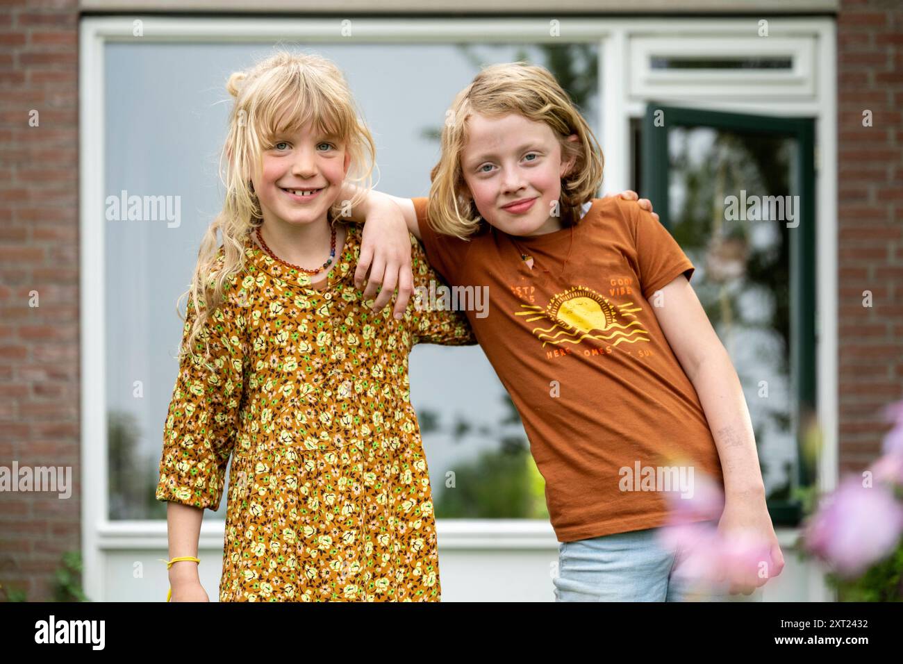Two smiling girls embracing each other in front of a house with a large ...