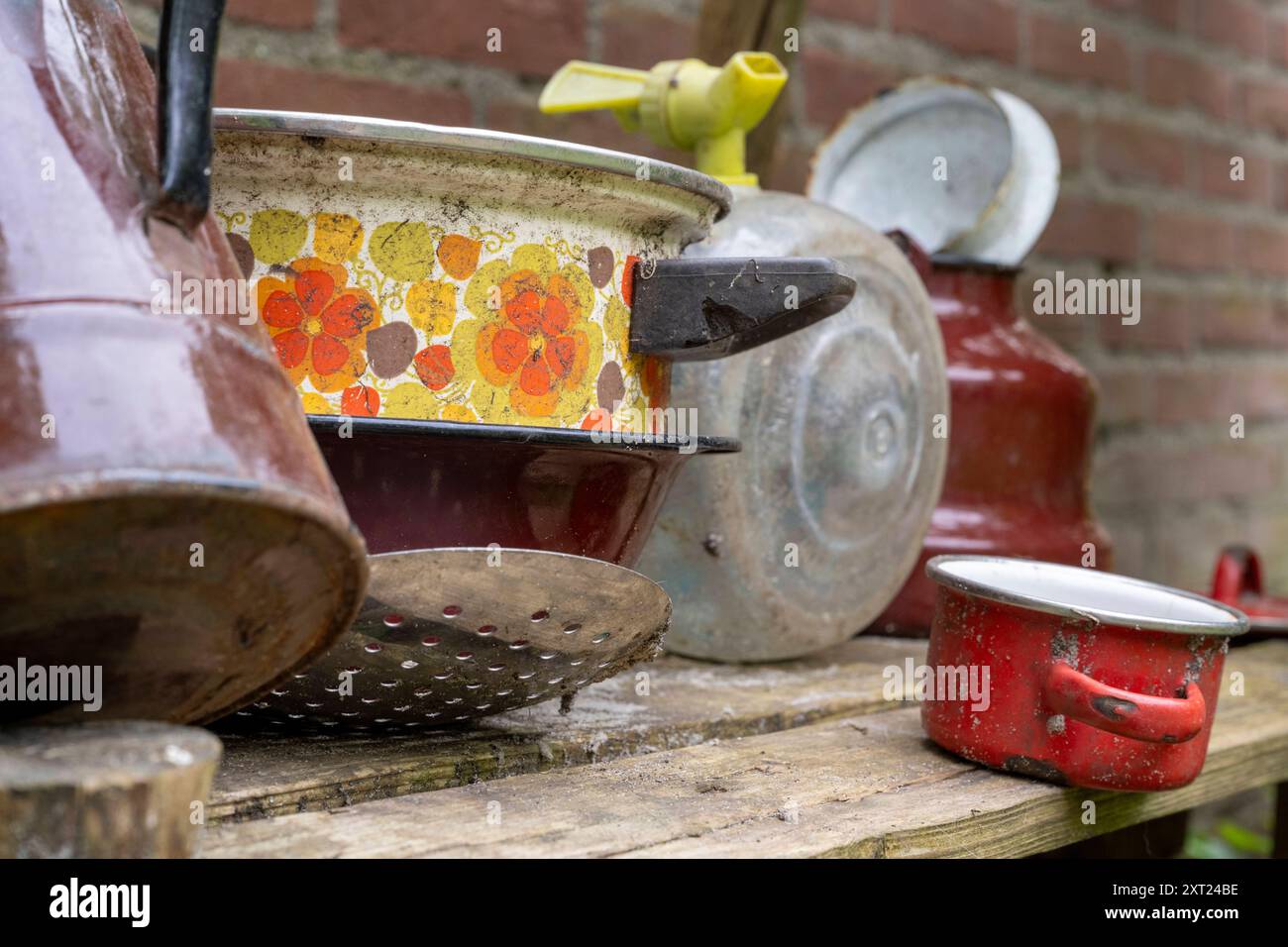 Old and rusty kitchen utensils on a worn wooden shelf against a brick ...