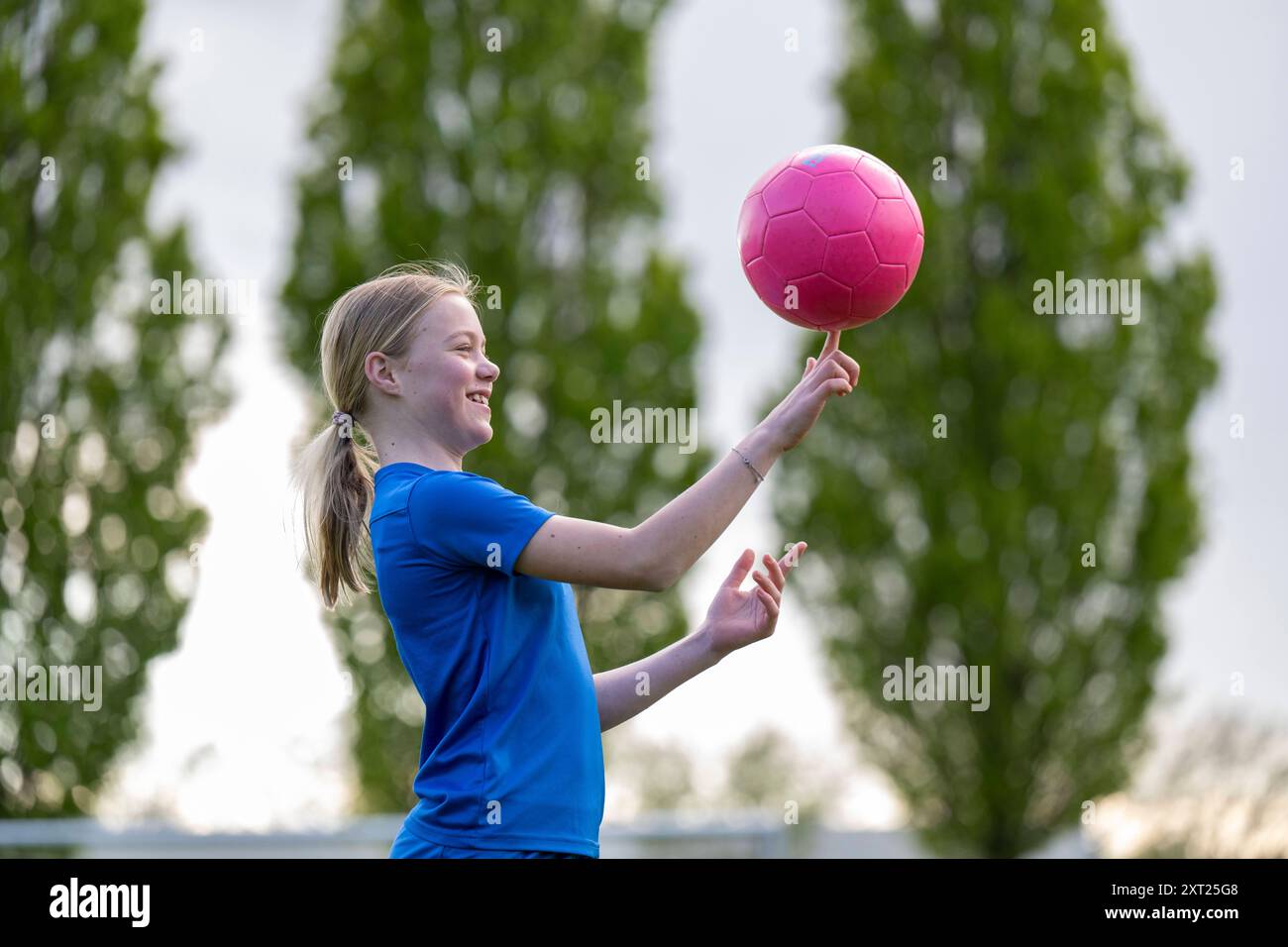 Girl in blue shirt playing with a pink ball outdoors against a green ...