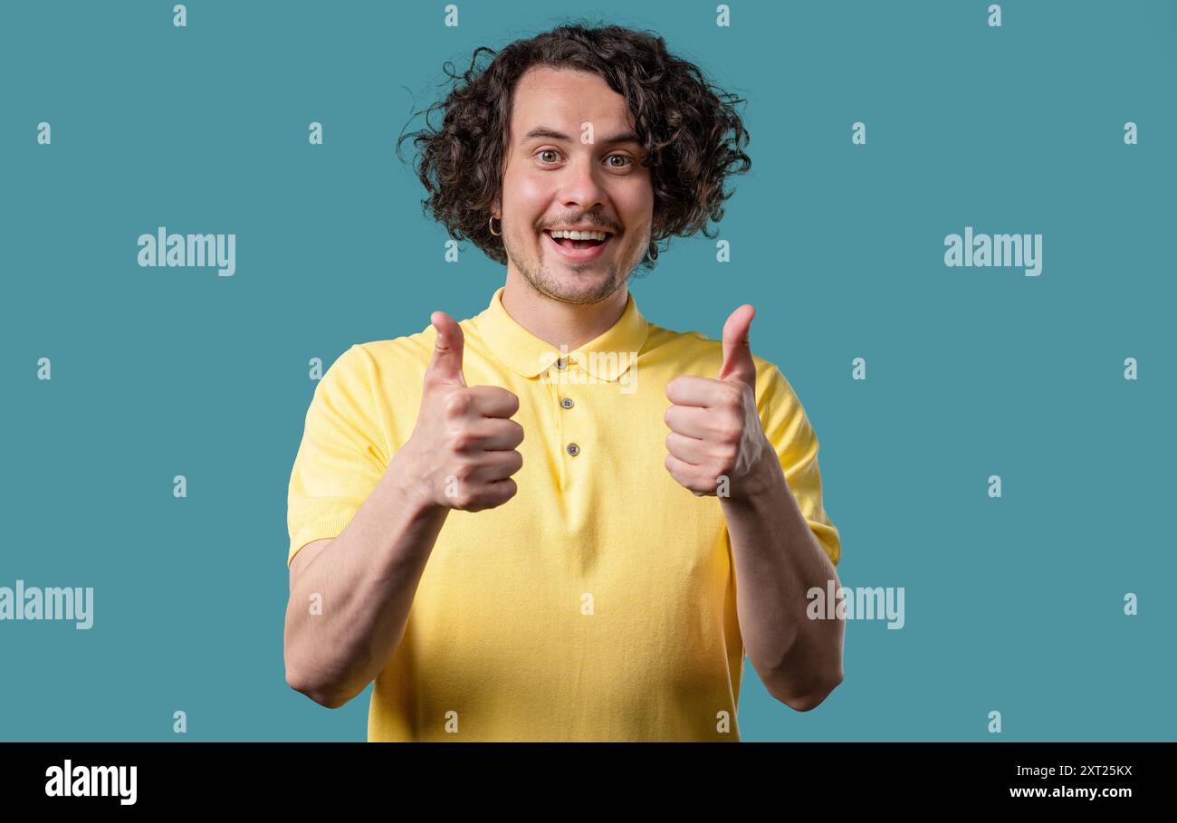 Happy hipster curly man with LIKE sign, thumbs up gesture. Blue studio ...