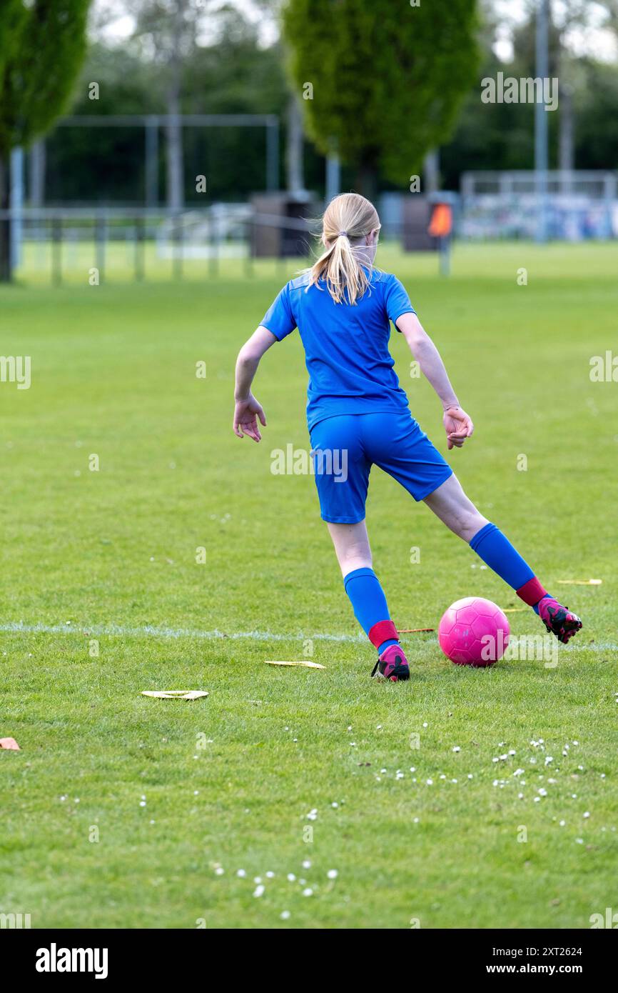 A female soccer player in a blue jersey dribbles a pink soccer ball on ...
