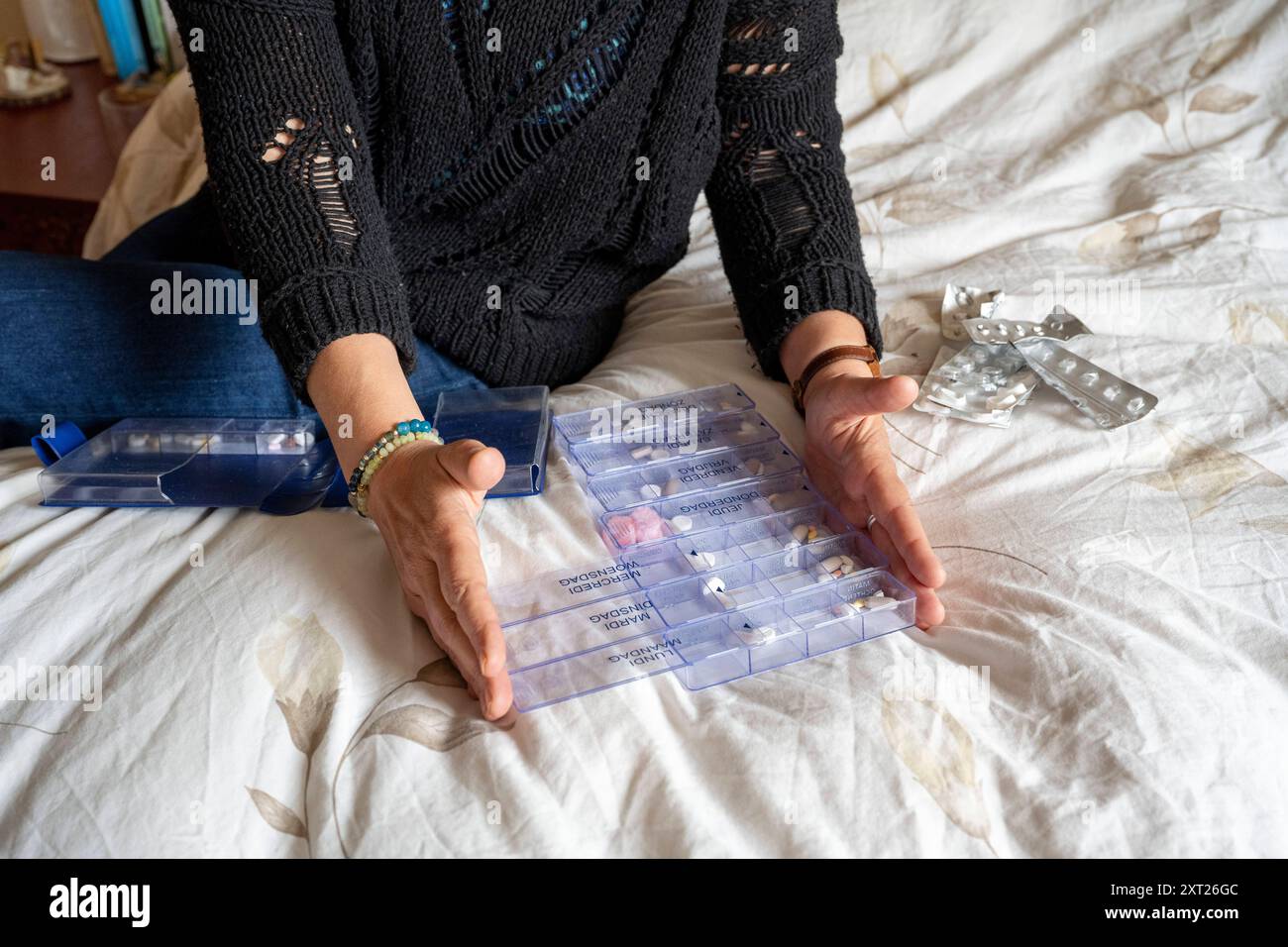 Hands of a seated adult carefully filling a weekly pill organizer from ...