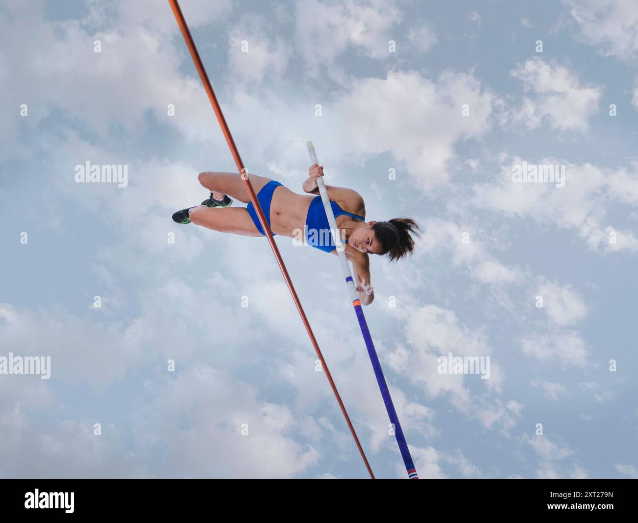 Female athlete vaulting over a high bar against a cloudy sky background ...