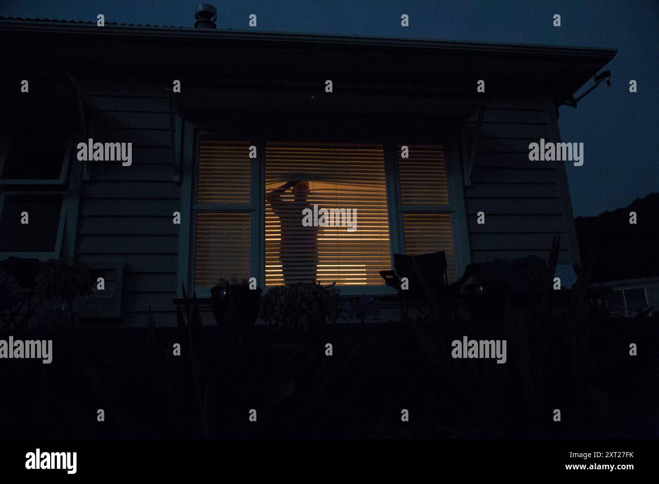 Silhouette of a person standing behind a window with blinds at night ...