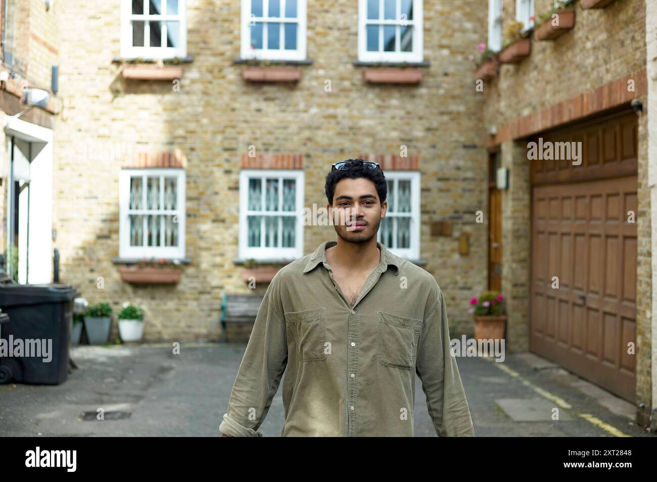 Young man standing in front of a brick house lined with windows and ...