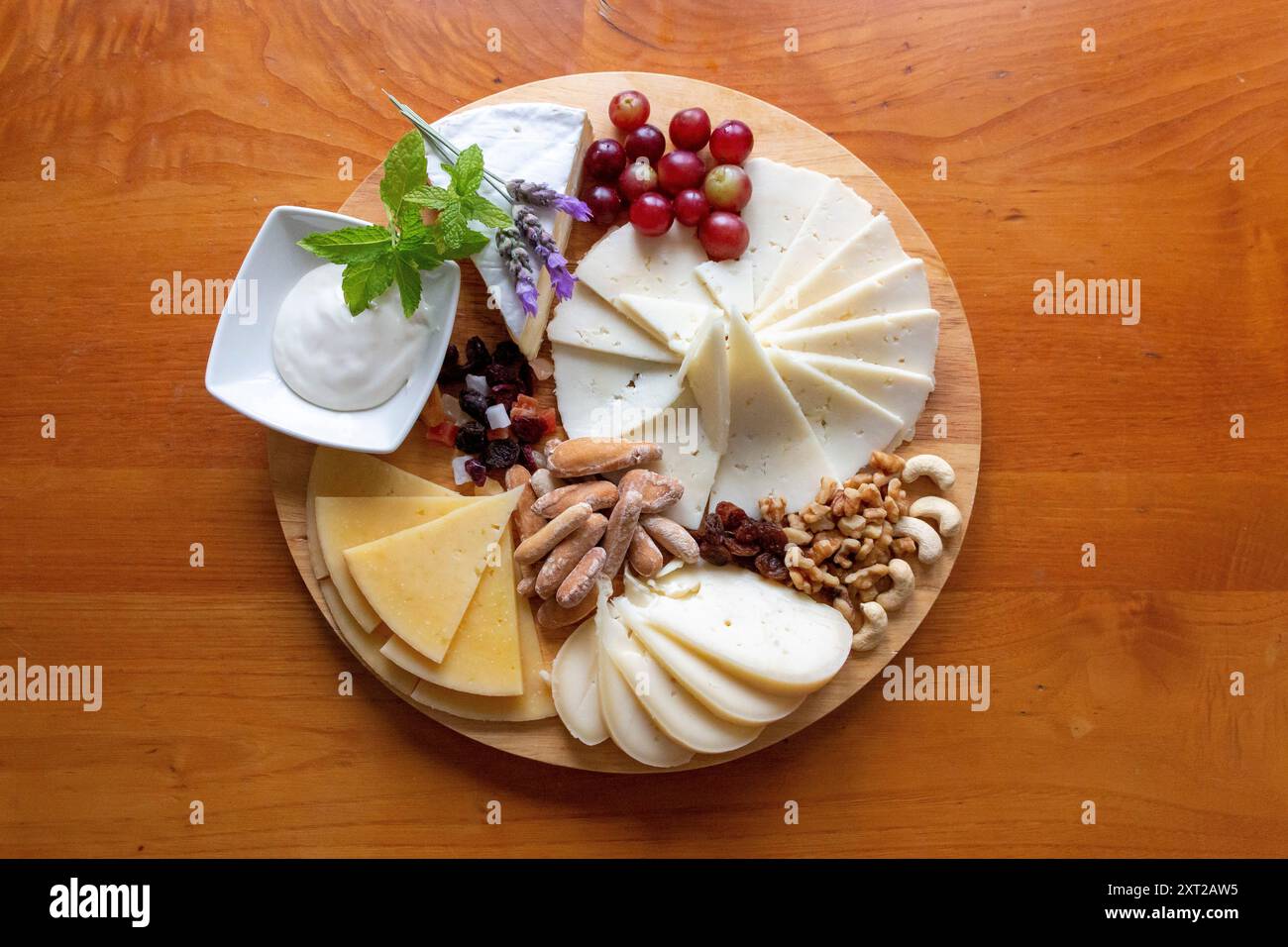 Table of different cheeses presented with grapes, nuts, some mint ...