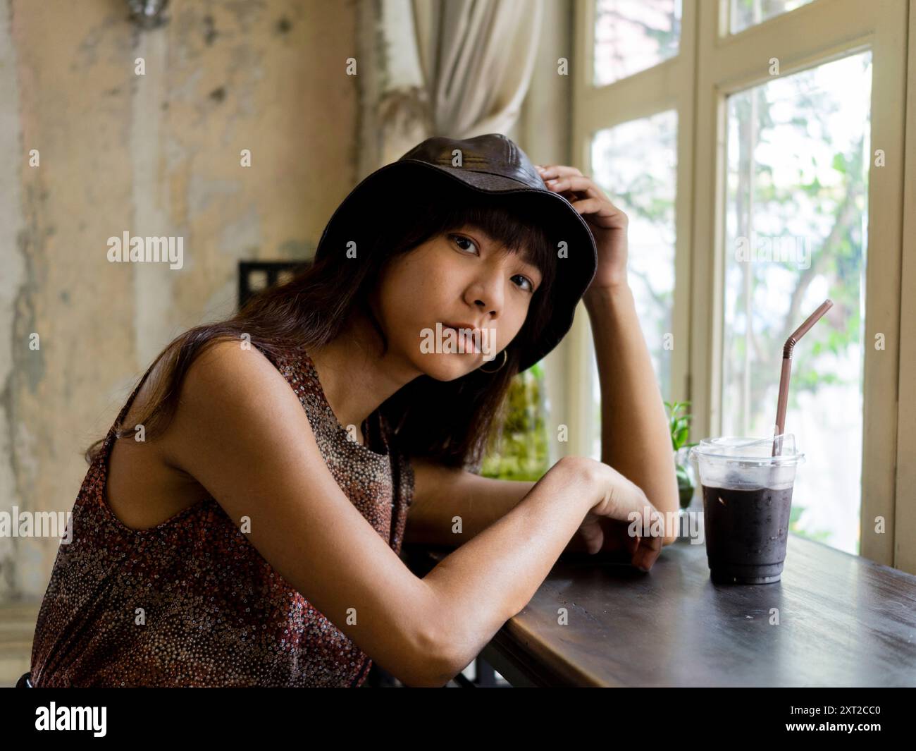Young asian woman wearing hat looking out of a cafe's window warm ...