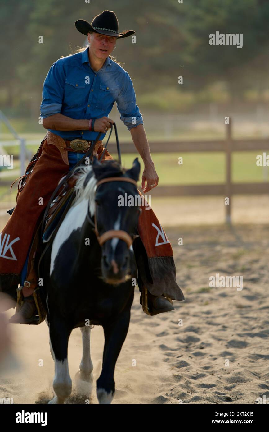Cowboy riding a black horse in a sandy arena during golden hour ...