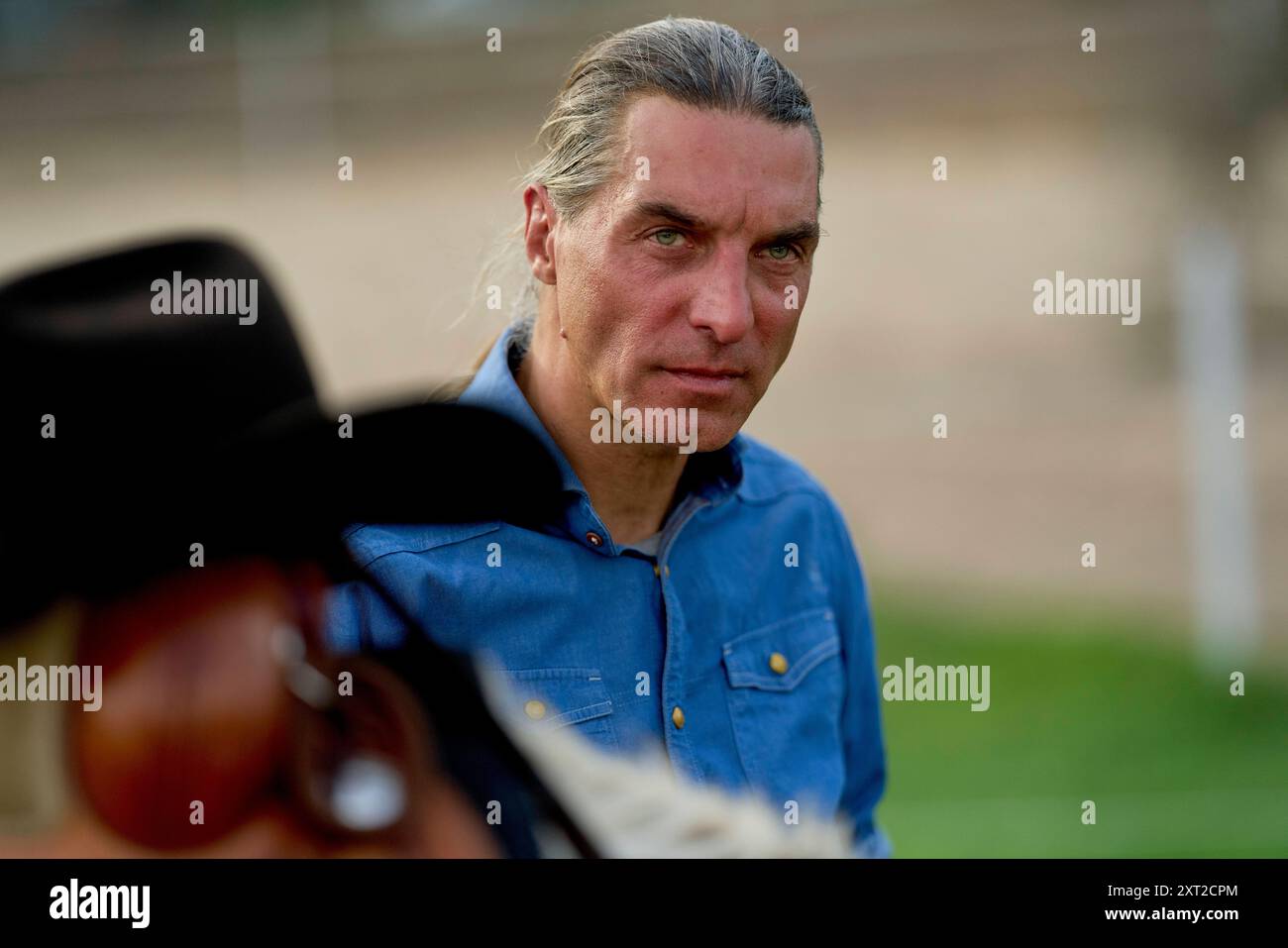 Man with grey long hair and blue shirt giving an intense stare behind a ...