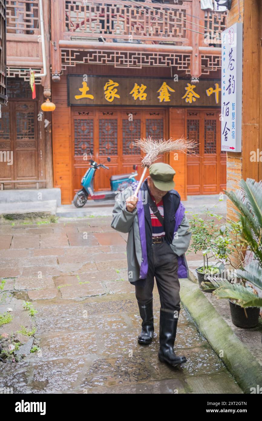 Elderly man sweeping wet cobblestone streets in a traditional Chinese ...