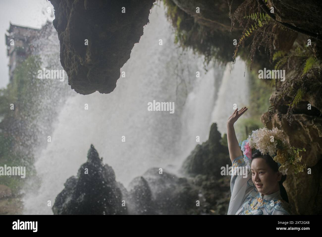 Woman in traditional attire posing near a waterfall surrounded by ...