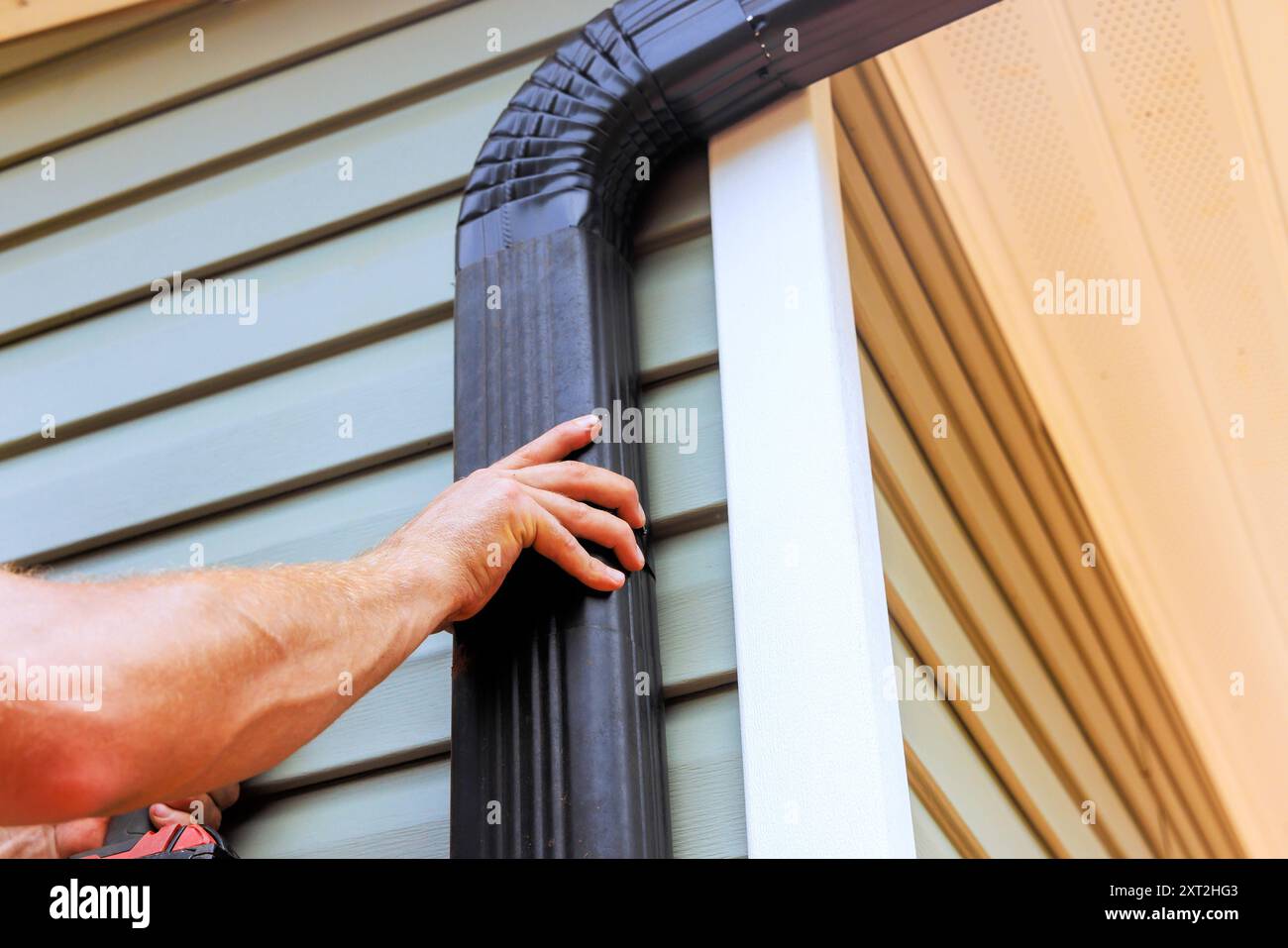 On roof, worker is installing rain gutter fitting downpipe downspout ...