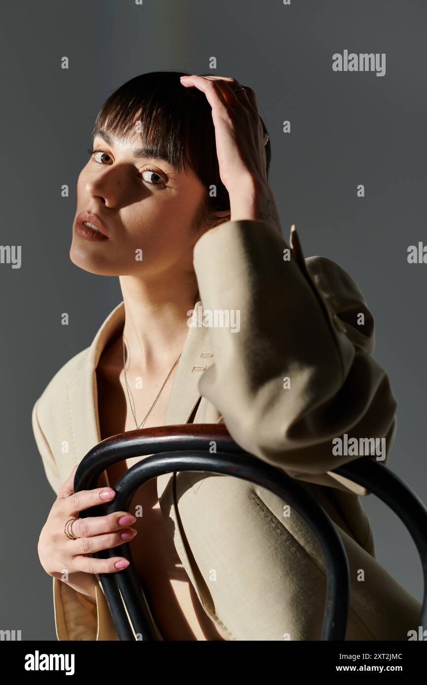 A young woman poses, hand resting on her head, against a backdrop of ...