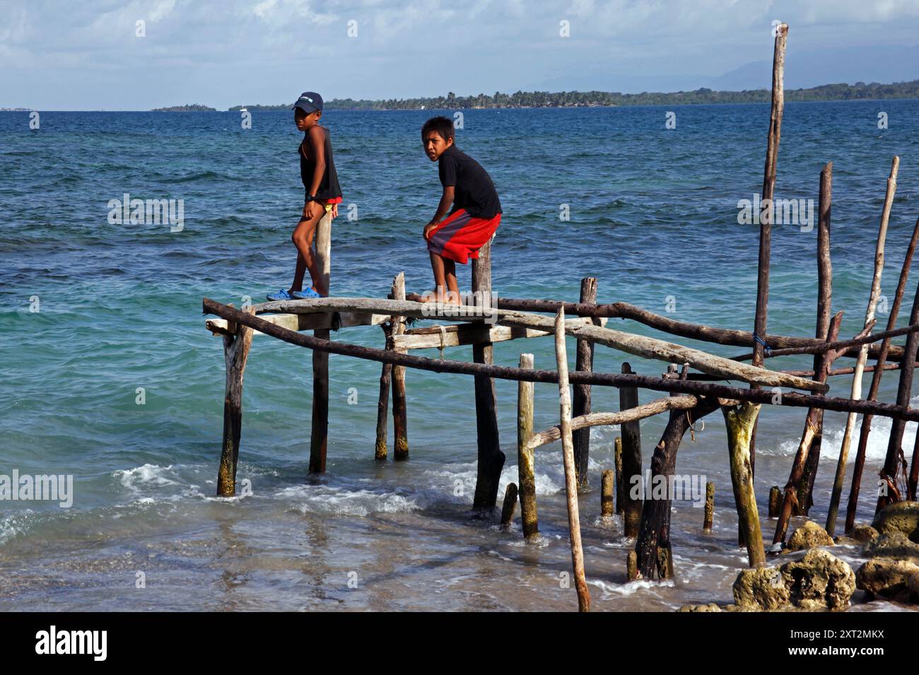 Kuna boy stting on rustic jetty made of wooden poles, sticks and beams ...