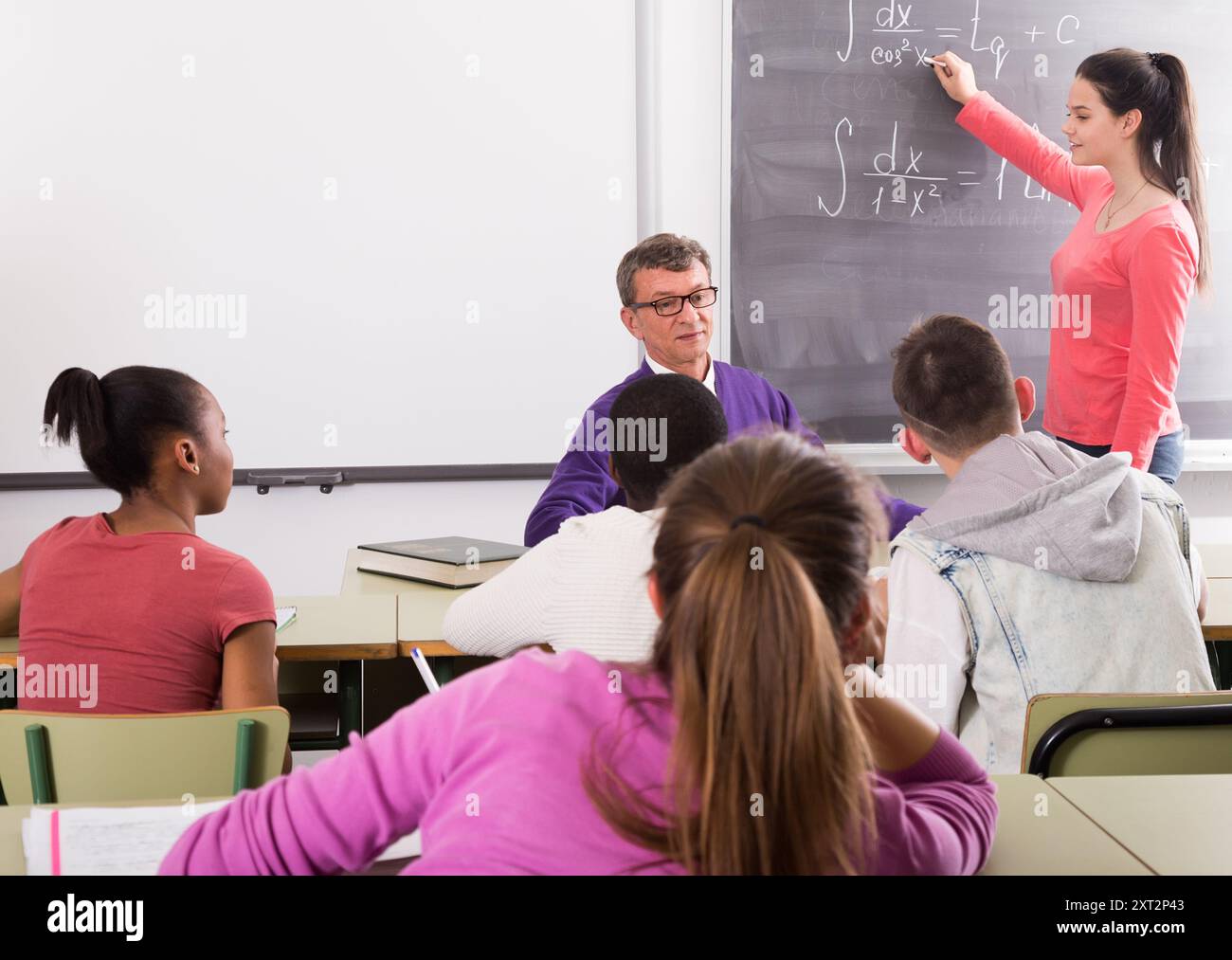 Cute student girl solves task near blackboard in classroom mathematics ...
