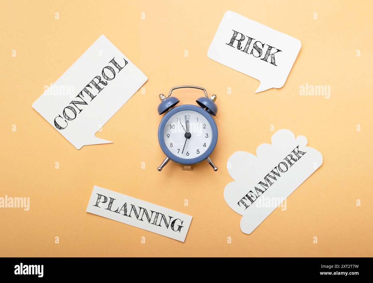 A clock sits on a table with a bunch of paper words around it. The ...