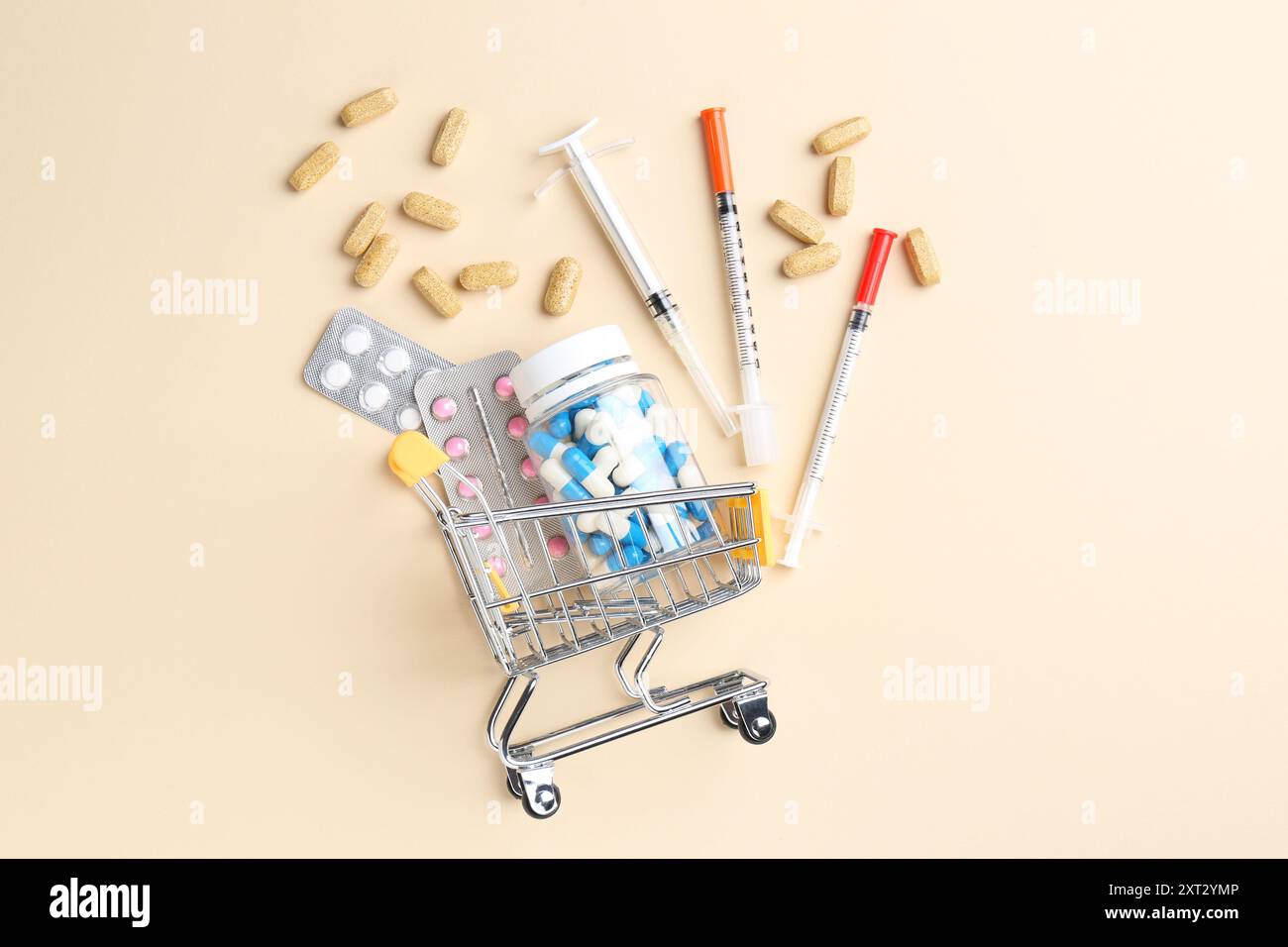 Pharmacist concept. Small shopping cart, syringes and pills on beige ...