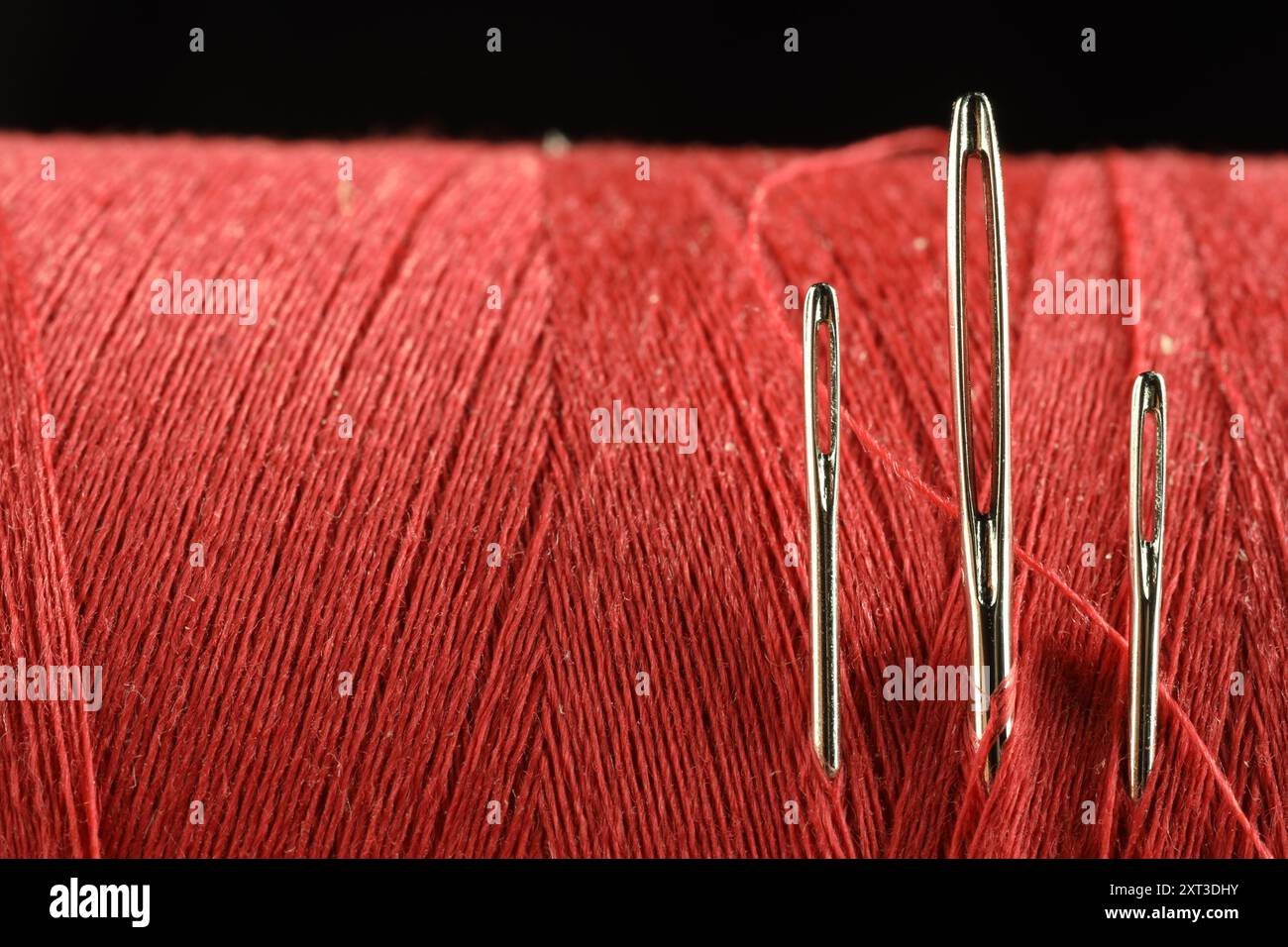 Spool of red sewing thread with needles on black background, macro view ...