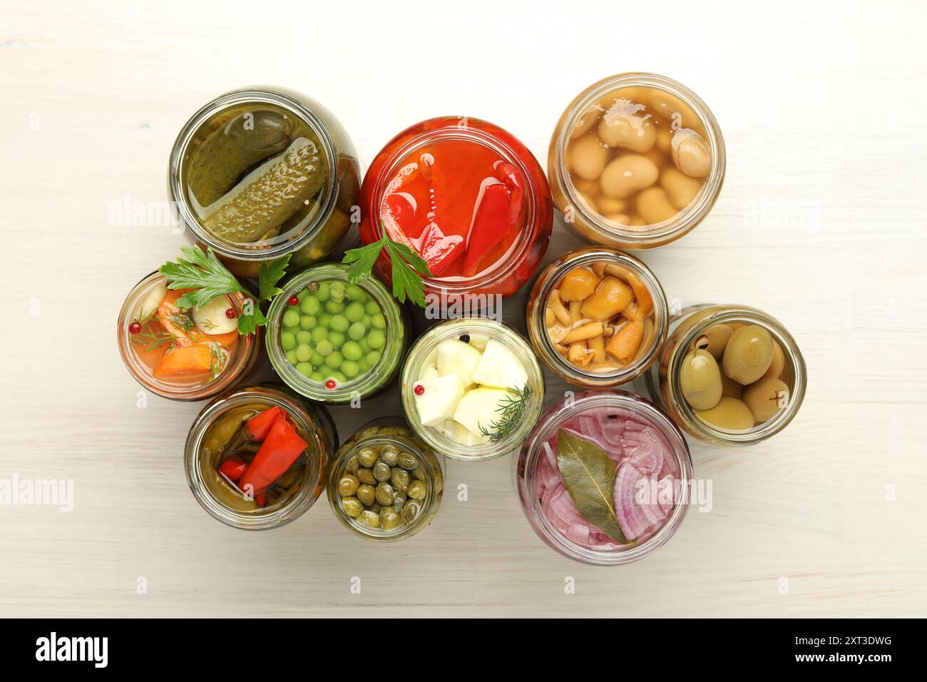 Different pickled products in jars on light wooden table, top view ...