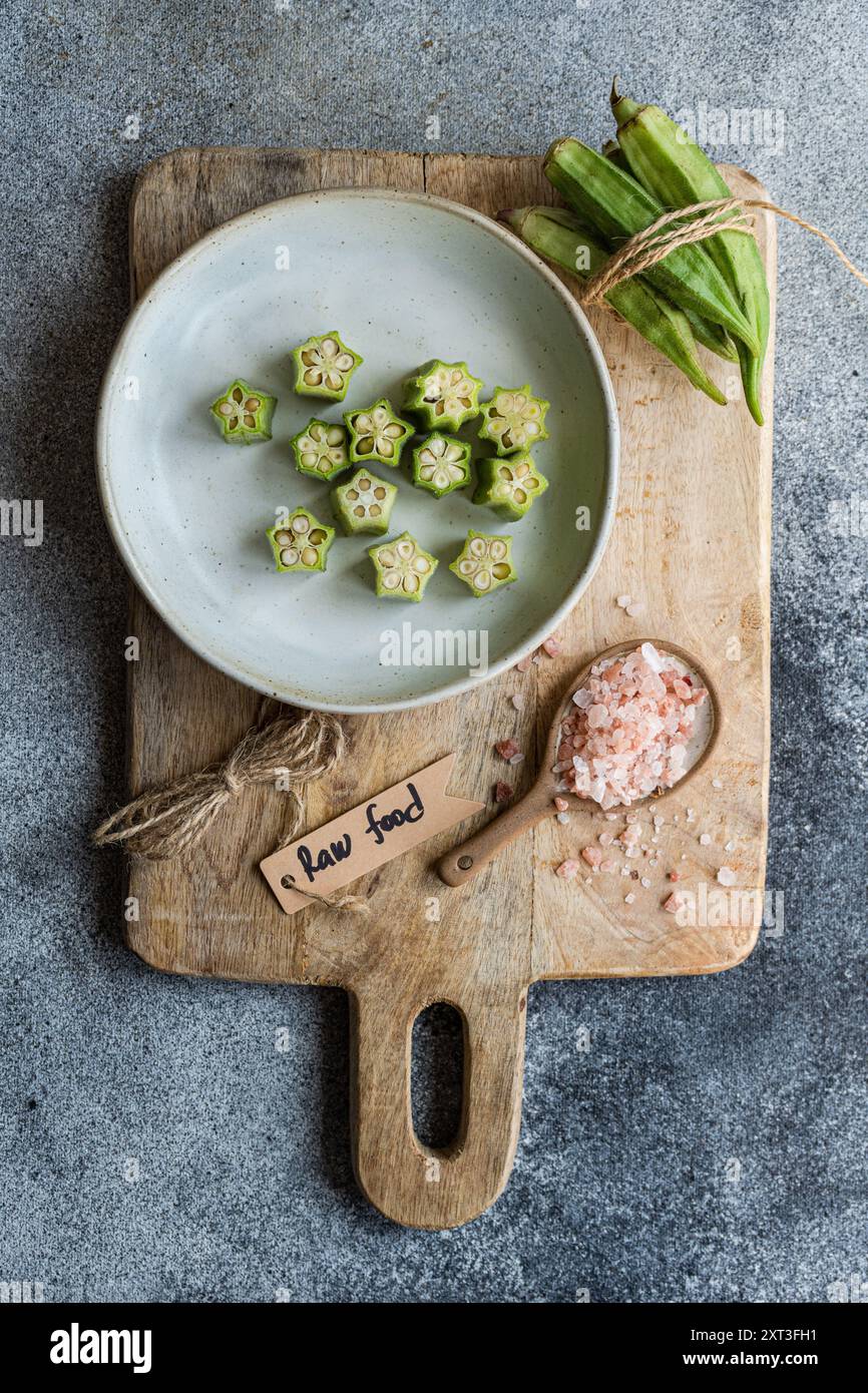 Raw, sliced bamia displayed on a rustic wooden board, accompanied by a ...