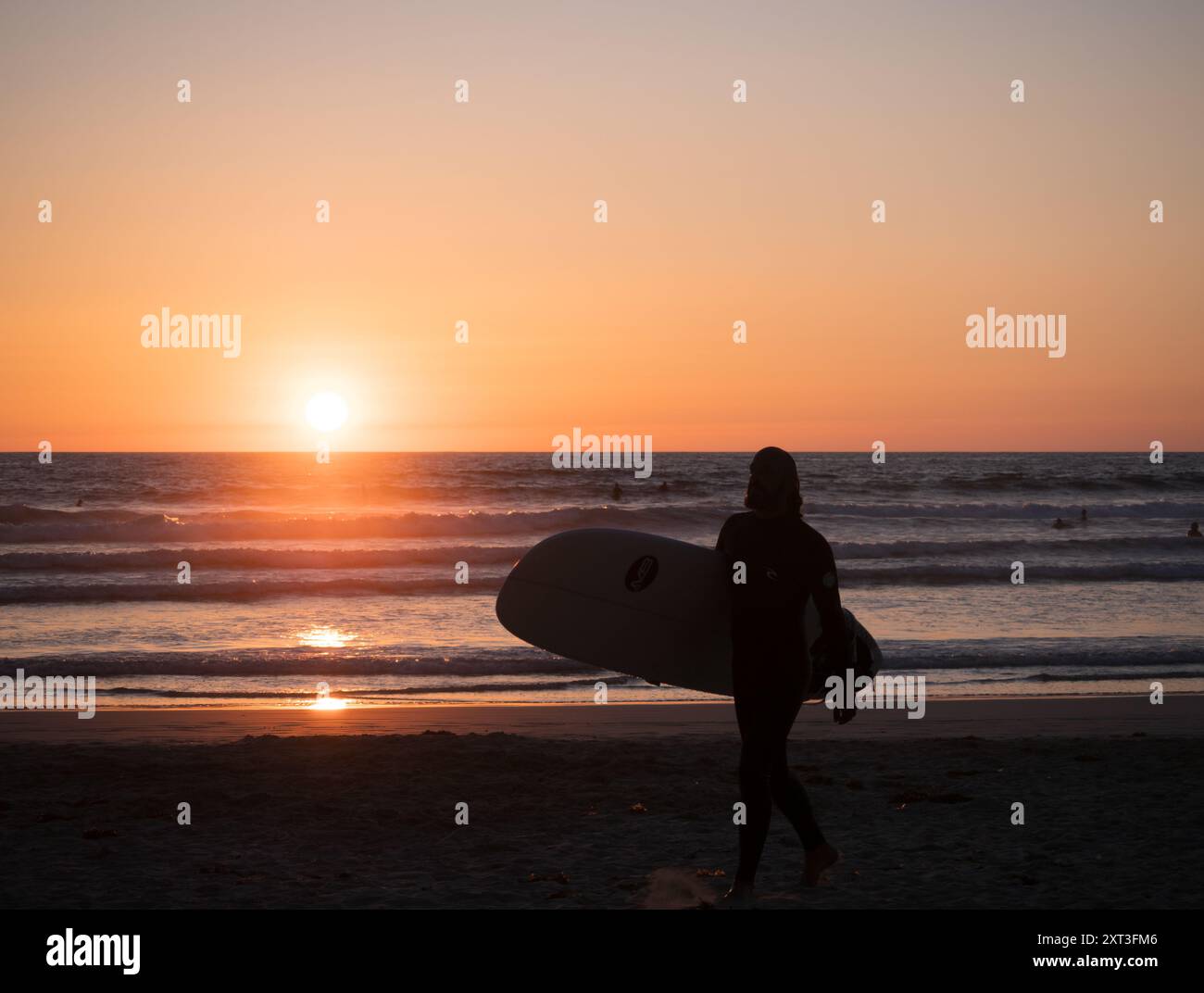 La Torche beach, France; August 10th 2024: A sufer walks on the beach at sunset after surfing ...