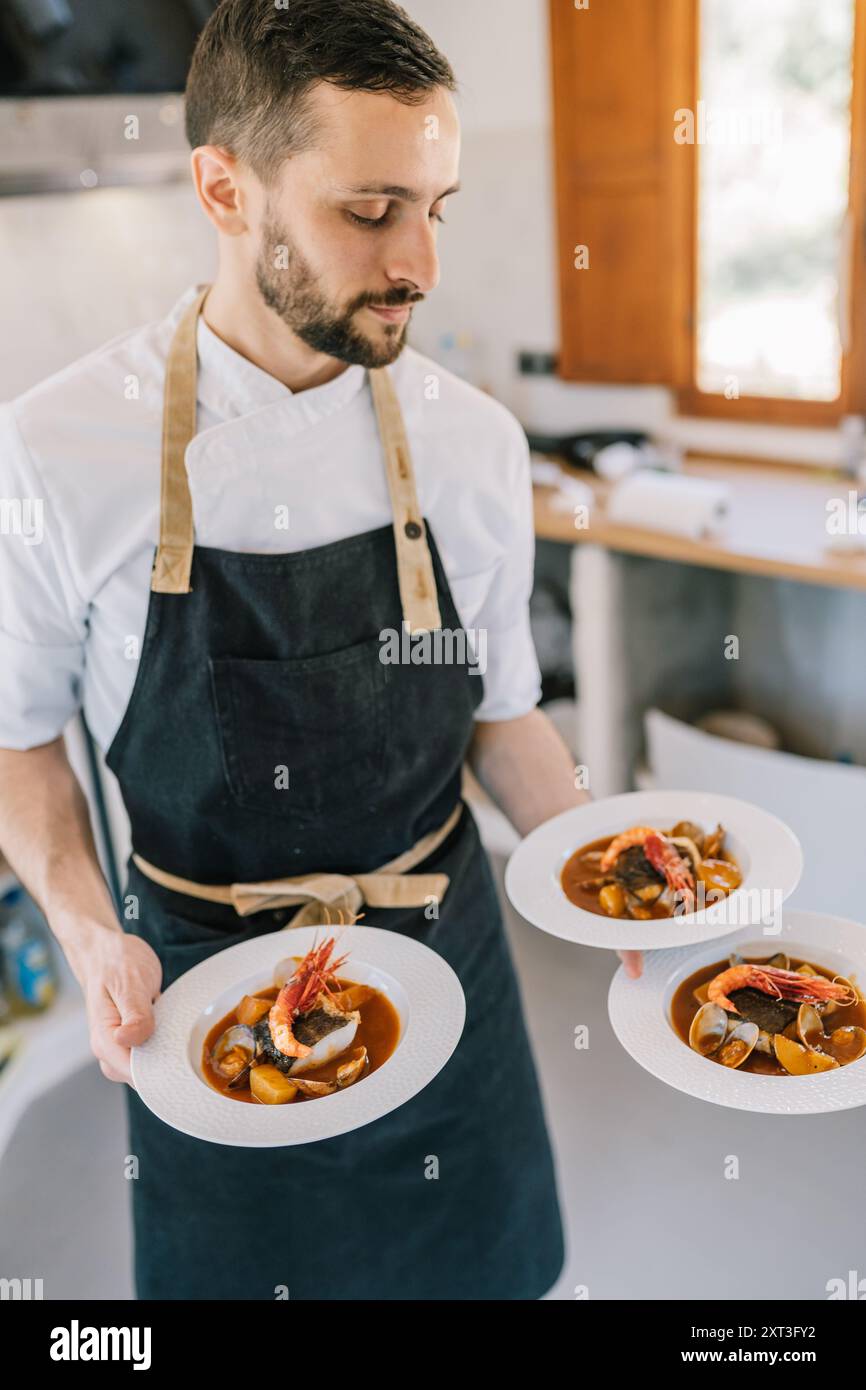 A focused private chef in apron, looking down, serving gourmet seafood ...
