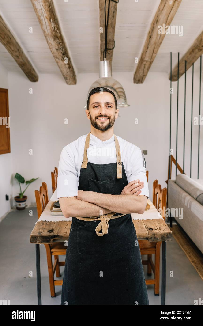 A cheerful male chef stands confidently in a cozy, rustic kitchen ...