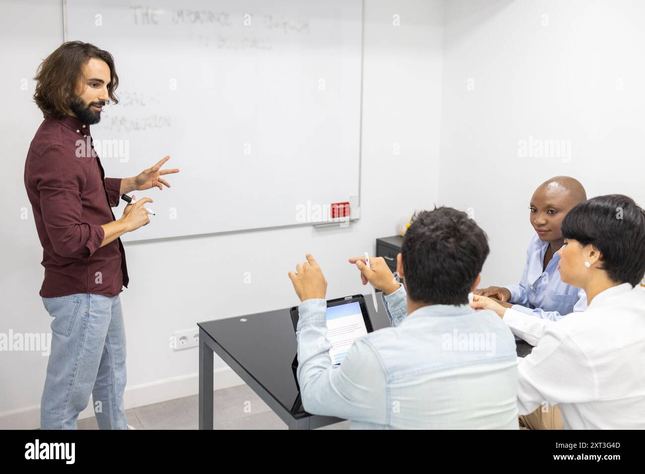 In a brightly lit classroom, a male teacher gestures animatedly while ...