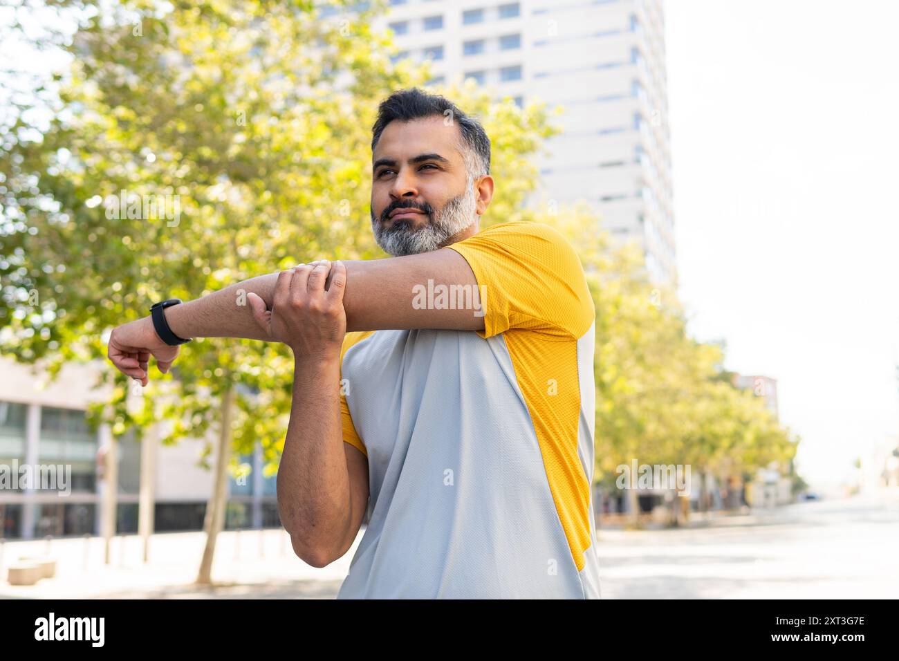Indian man in yellow sports shirt stretching arm on urban background ...