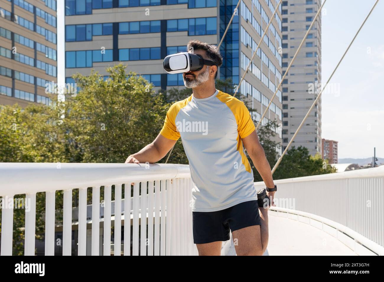Indian man wearing a virtual reality headset stands on a city bridge ...