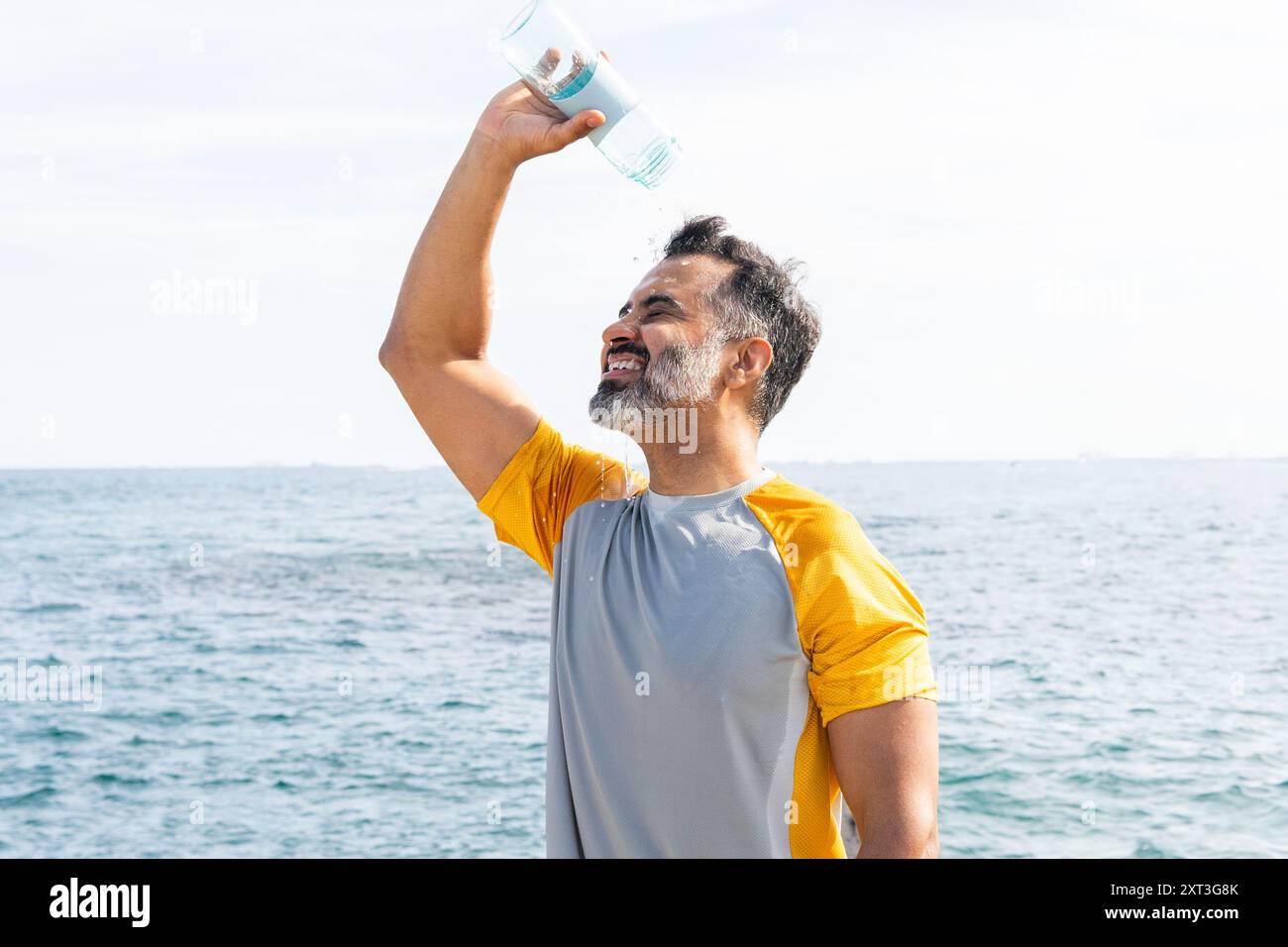 An Indian man pours water over his face from a clear bottle, on a sunny ...