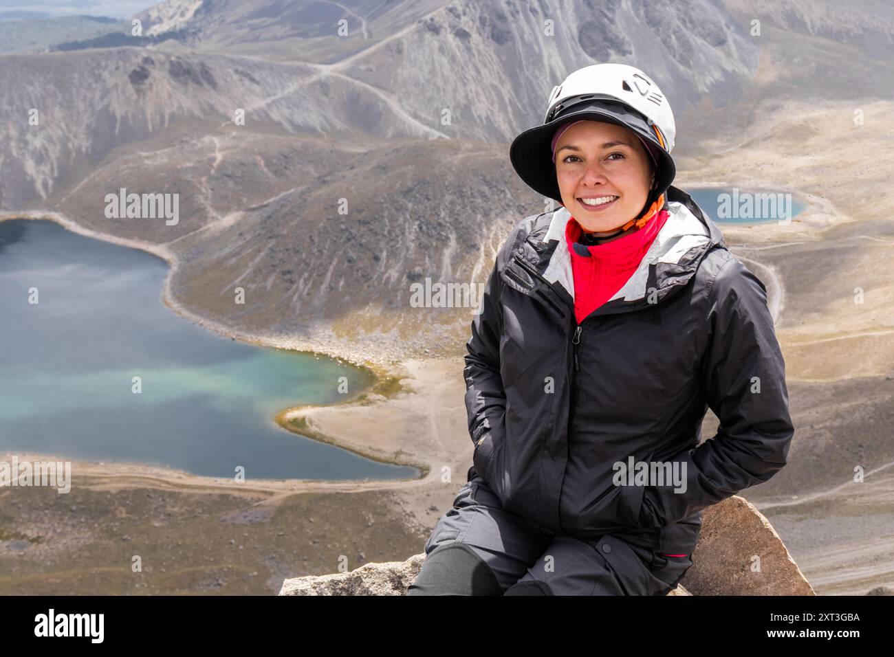 A happy hiker, Latin Hispanic female, sits atop a rocky outcrop ...