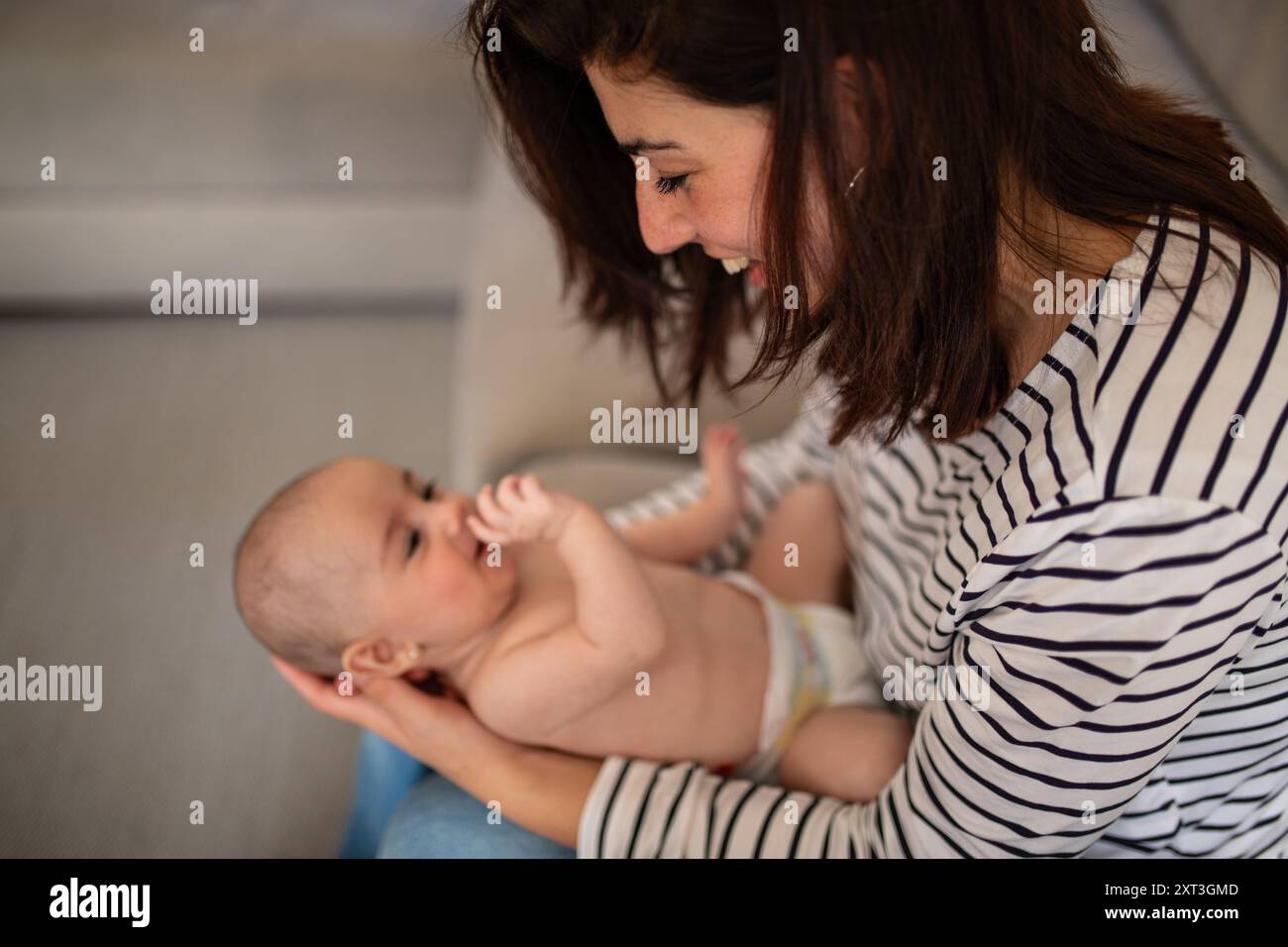 A loving mother in a striped top smiles warmly at her newborn baby ...